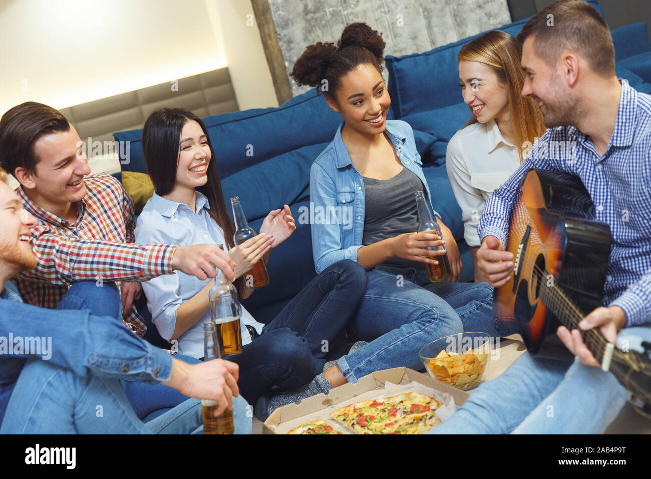 Group of friends having party indoors fun together guy playing guitar ...