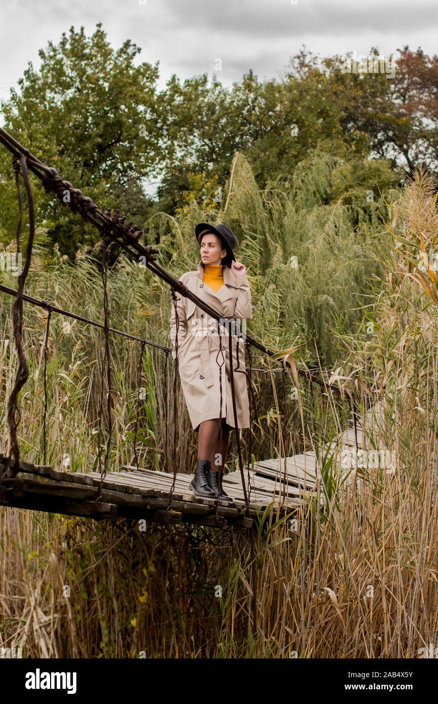 Beautiful girl on a suspension bridge. Woman in a black hat and a beige ...
