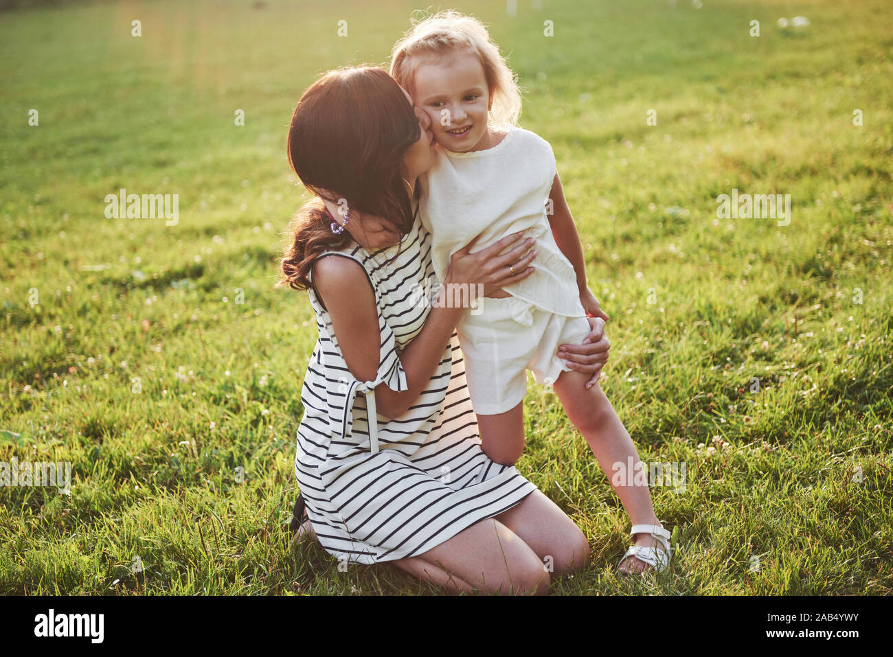Happy mother and daughter hugging in a park in the sun on a bright summer background of herbs ...
