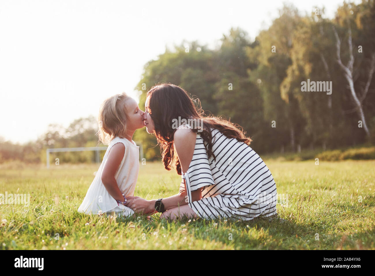 Happy mother and daughter hugging in a park in the sun on a bright summer background of herbs ...