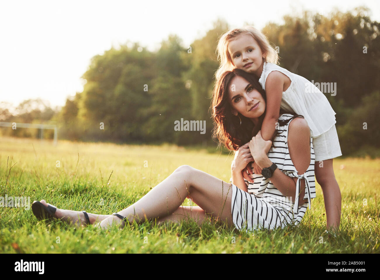 Happy mother and daughter hugging in a park in the sun on a bright summer background of herbs ...