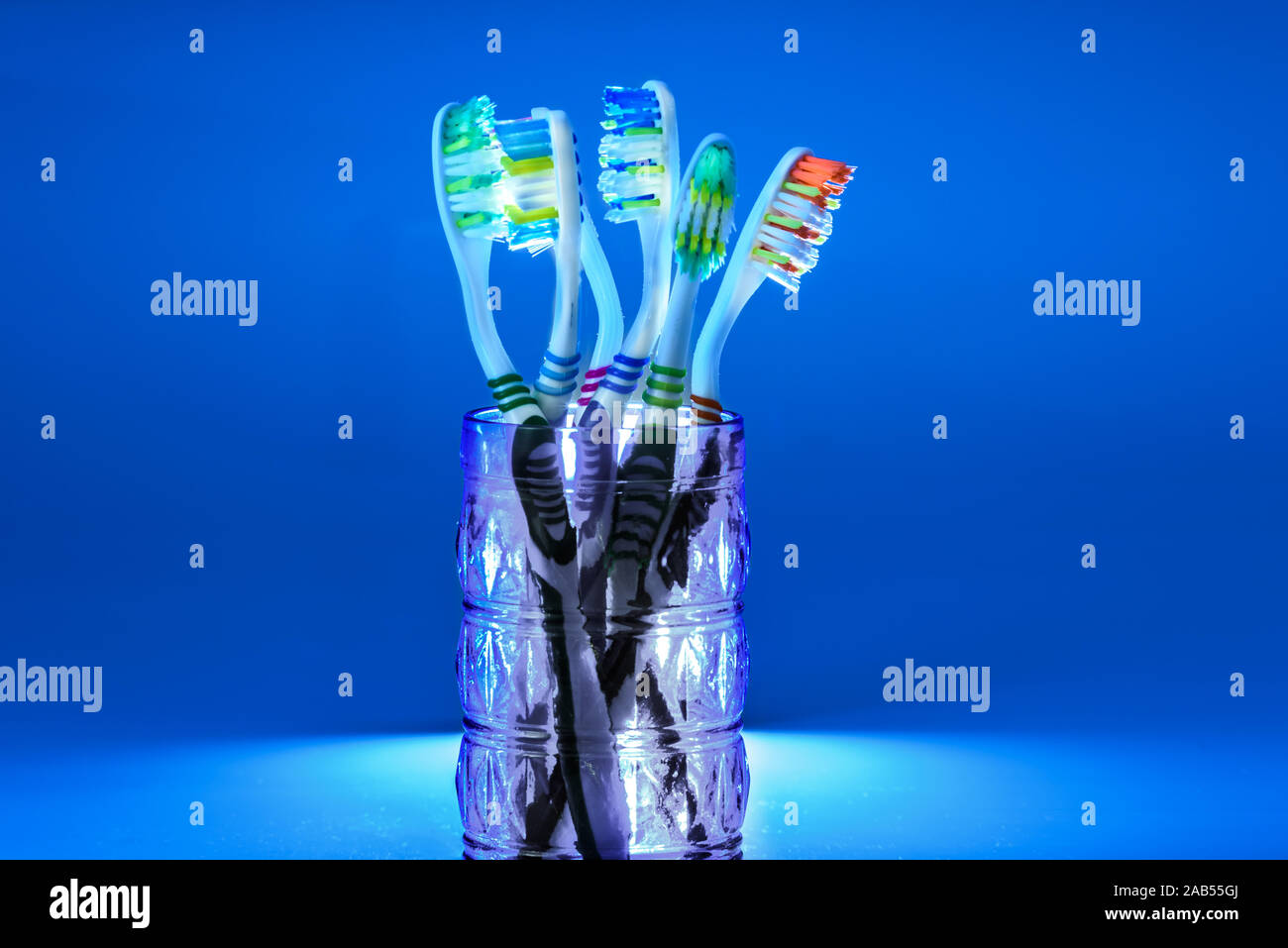 Many new plastic toothbrushes inside a glass, isolated on striking blue ...