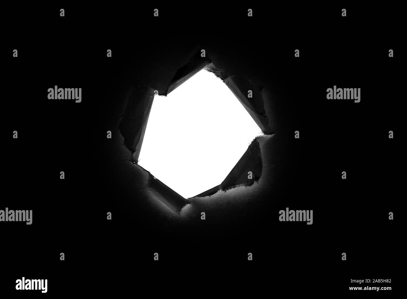 A round hole in black paper with torn edges isolated with a white ...