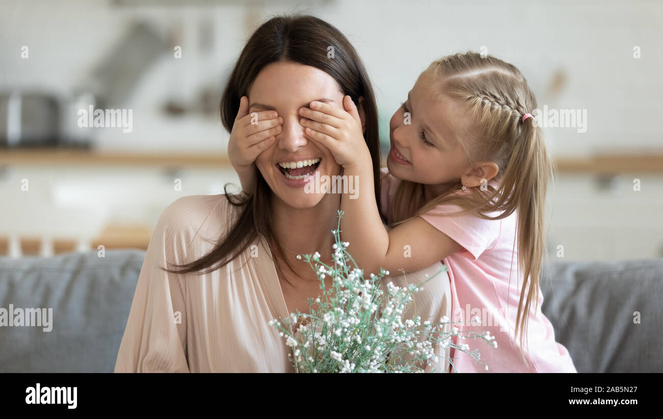 Child daughter make surprise close eyes of mommy presenting flowers ...