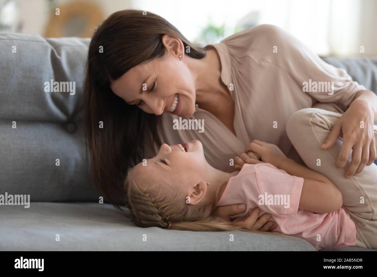 Smiling mother and little kid daughter playing tickling on sofa Stock ...