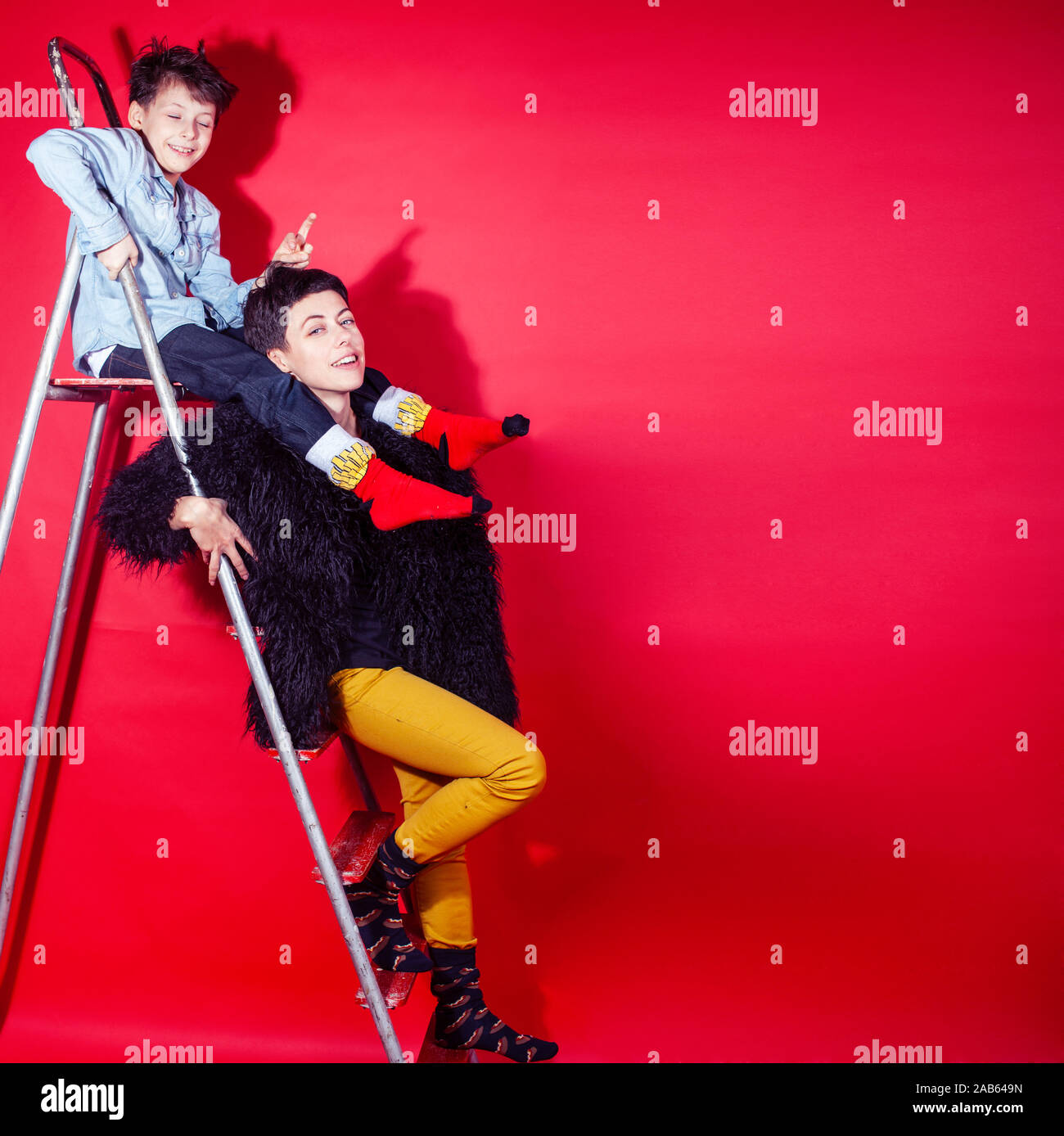 pretty young mother with little son on ladder on red background posing ...