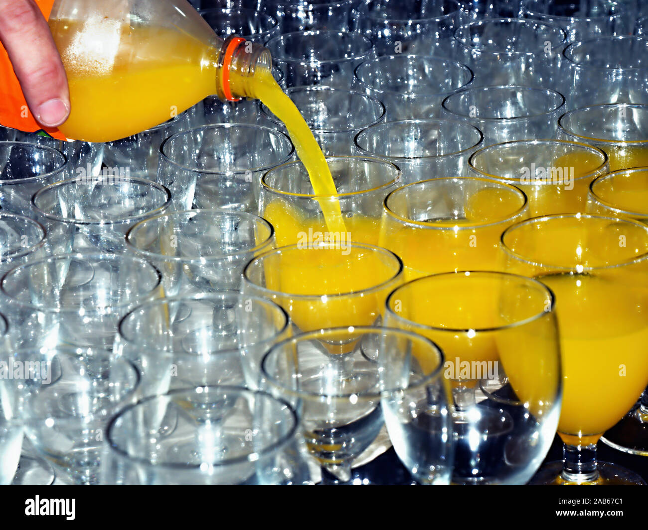 A yellow soft drink from a transparent bottle is poured into glasses ...