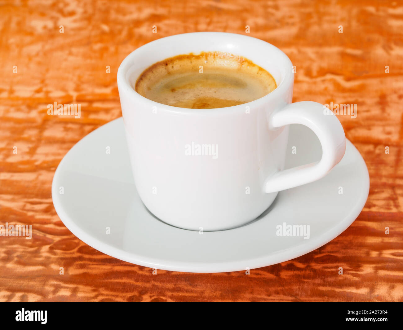 black frothy coffee with foam in white cup with plate on bright copper ...