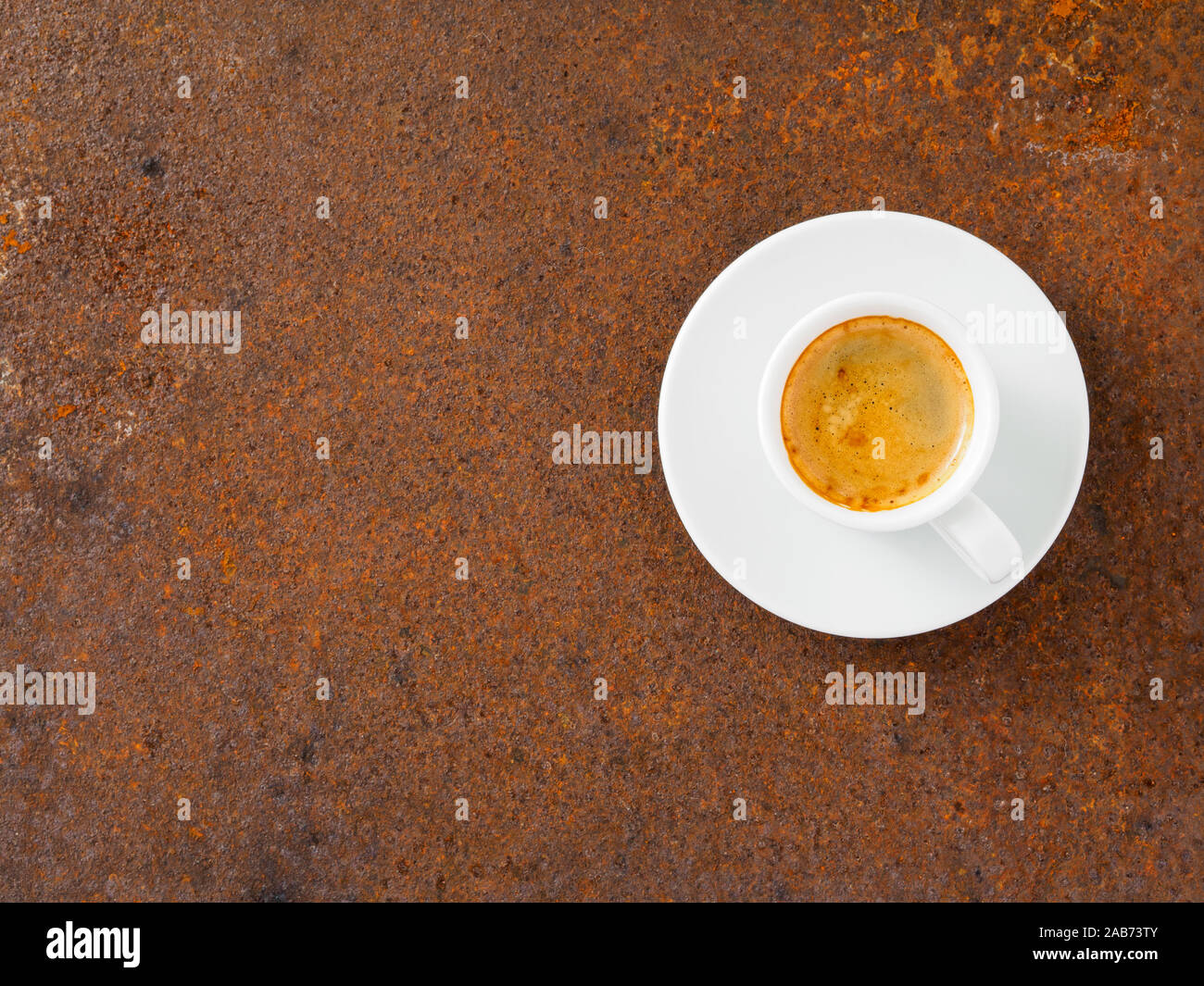 black frothy coffee with foam in white cup with plate on rusty metal ...