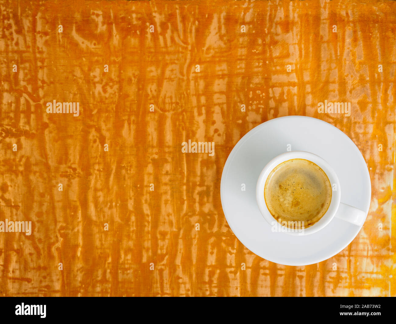 black frothy coffee with foam in white cup with plate on bright copper ...