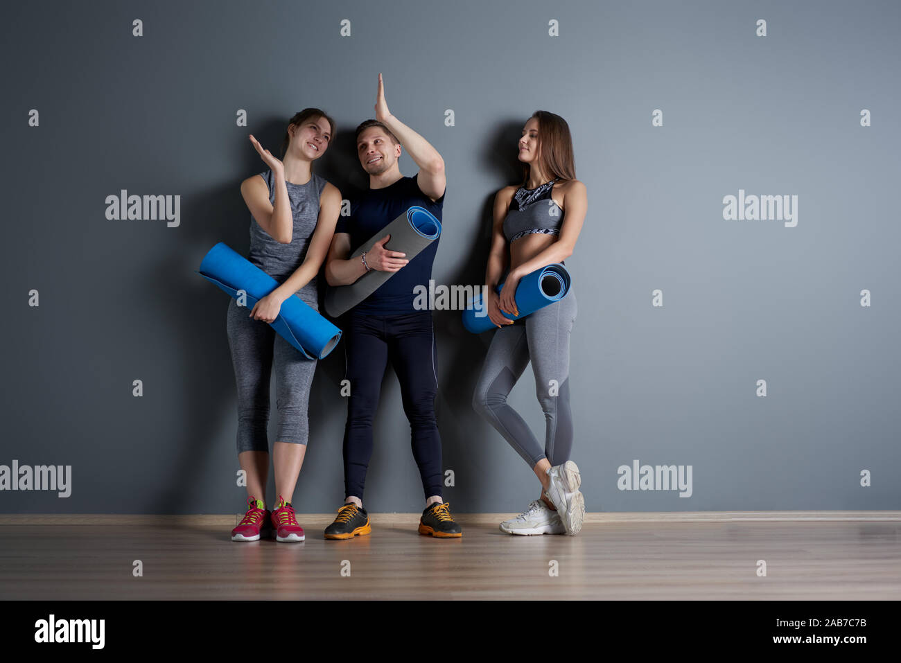 Sporty women shaking hands and man with twisted blue rugs against gray ...