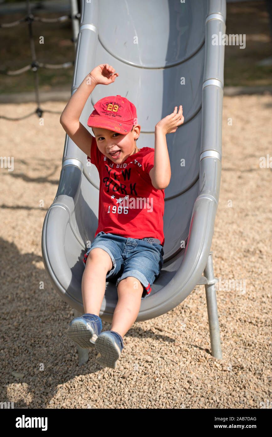 Boy with red hat and t-shirt playing on slide Stock Photo - Alamy