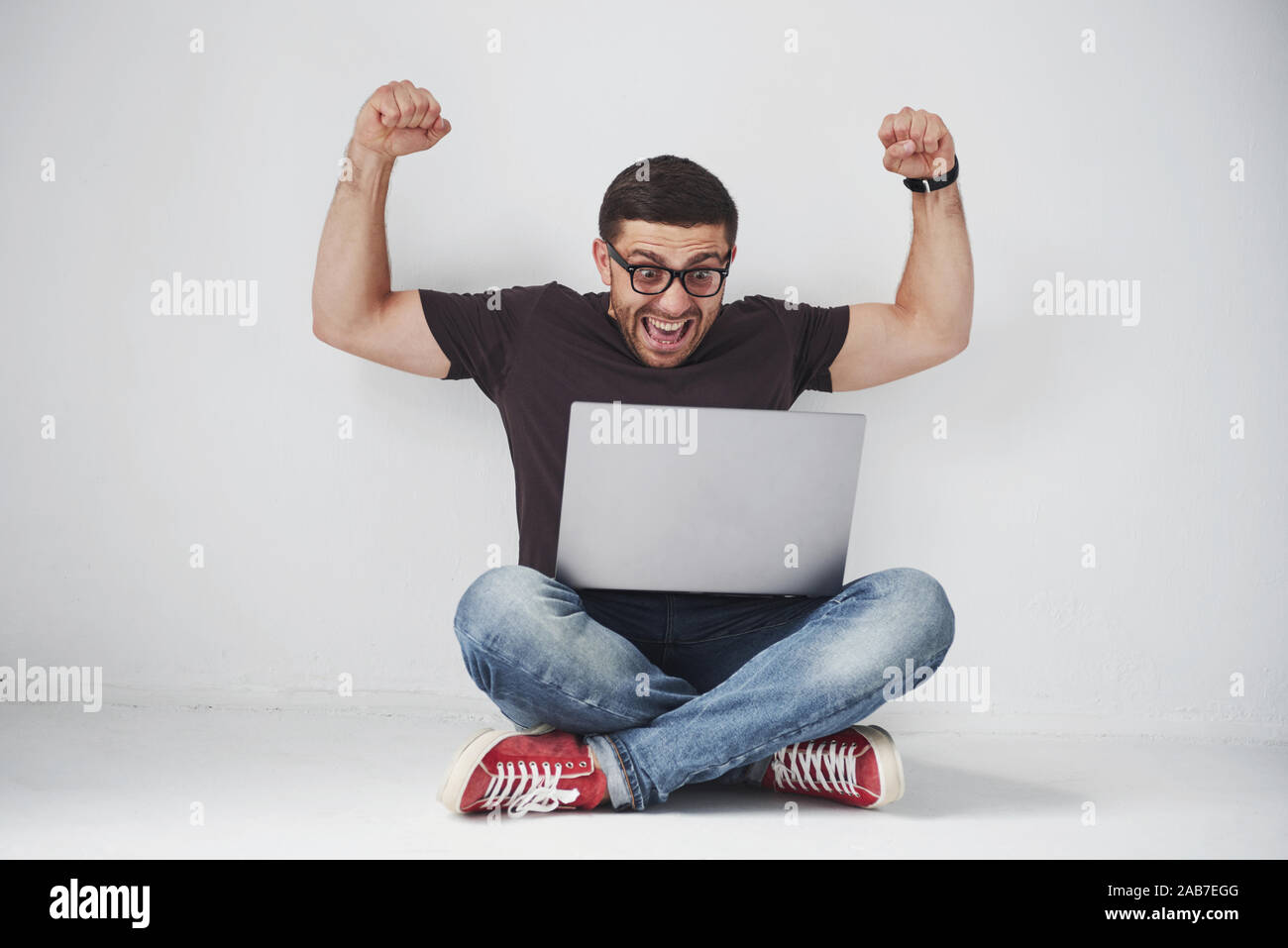 Young caucasian man sitting over white brick wall using computer laptop ...