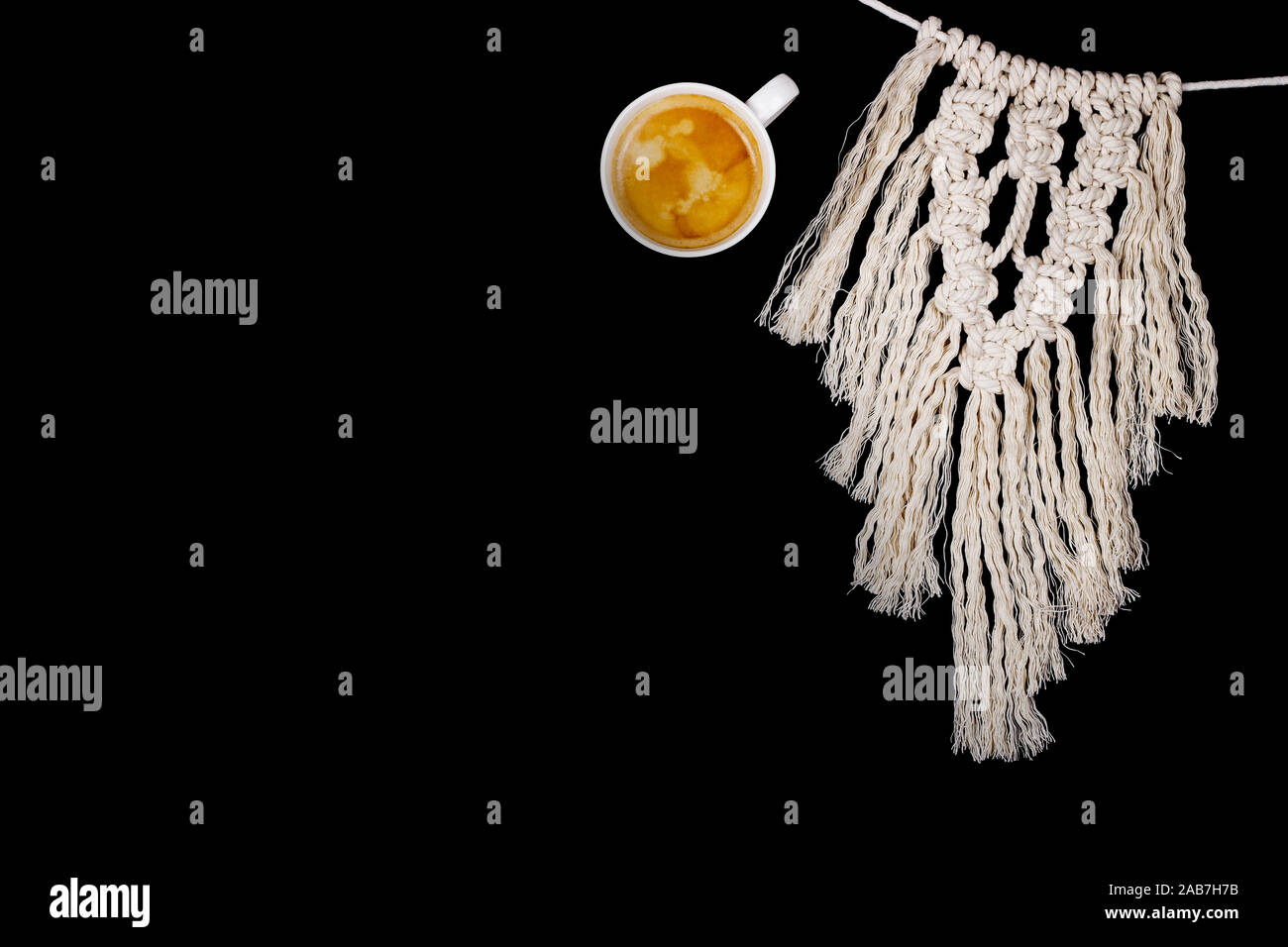 White macrame next to a cup of coffee with foam on a black isolated ...
