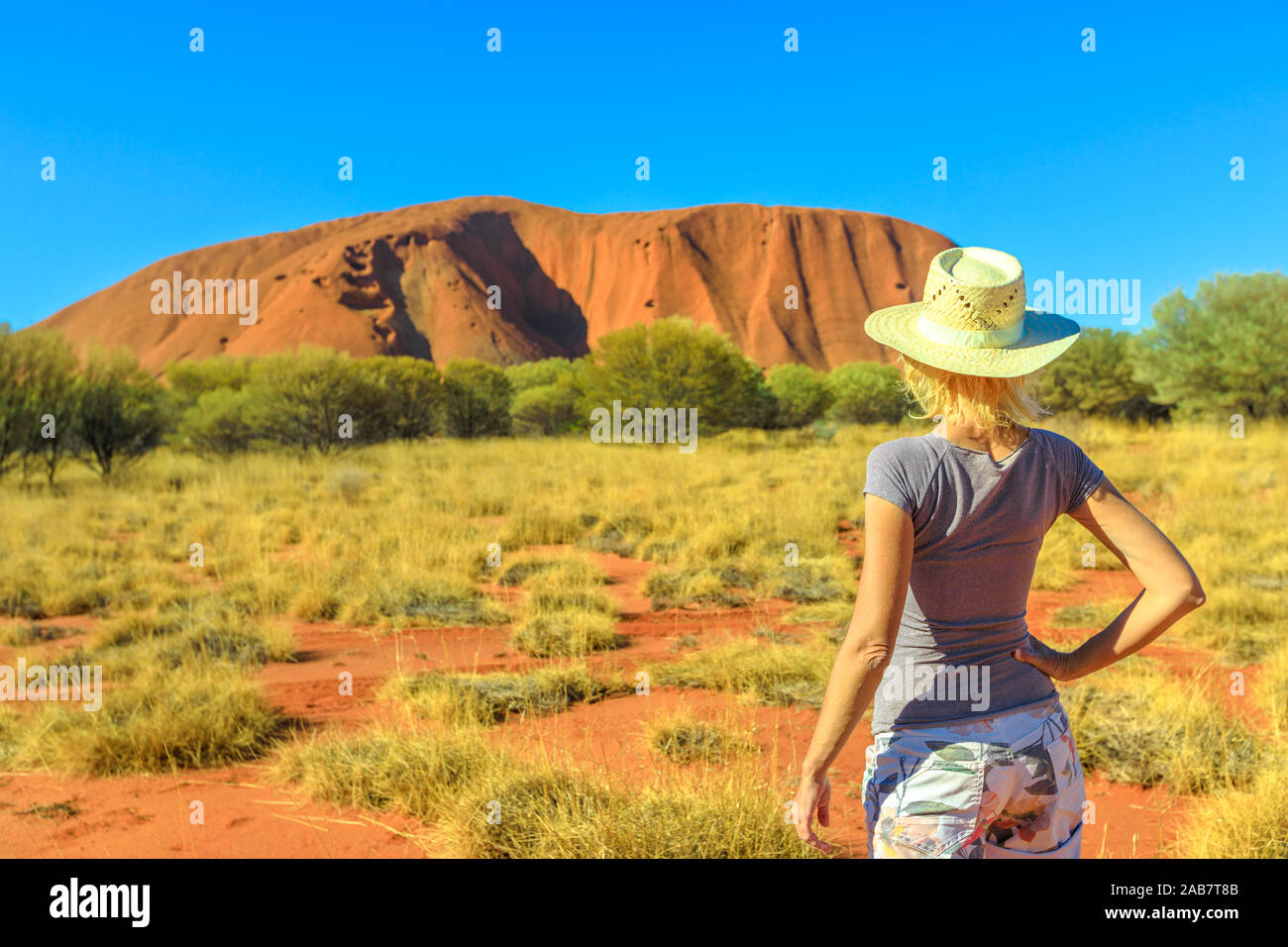 Tourist woman in hat looks at Uluru (Ayers Rock) in the dry season ...