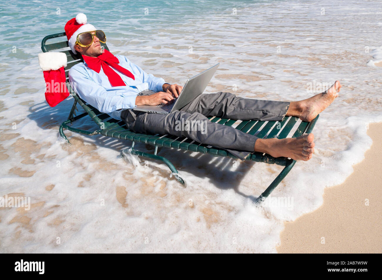 Happy barefoot Santa office worker working on his laptop on a tropical ...