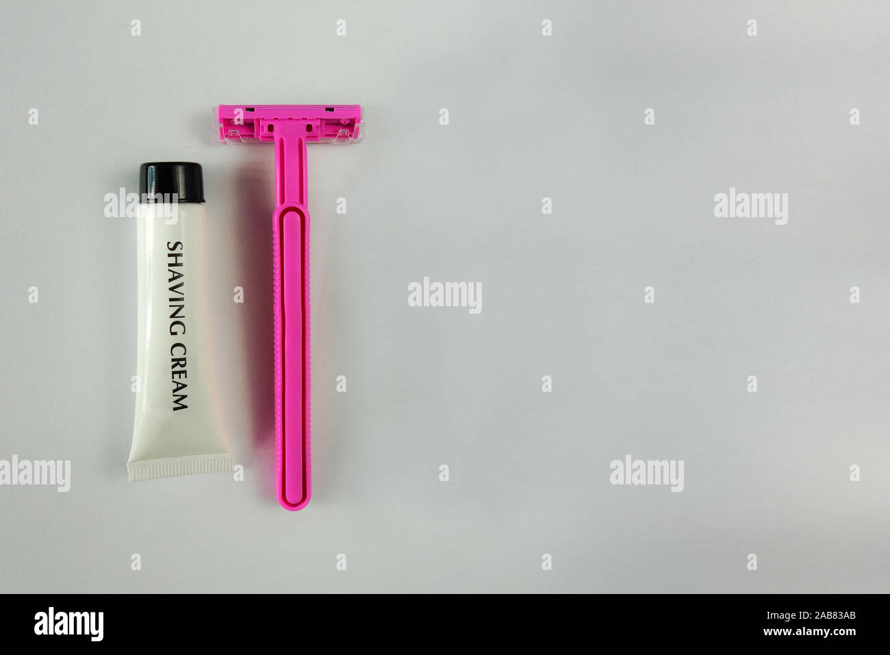 Pink shaving stick and white tube with shaving cream on light ...