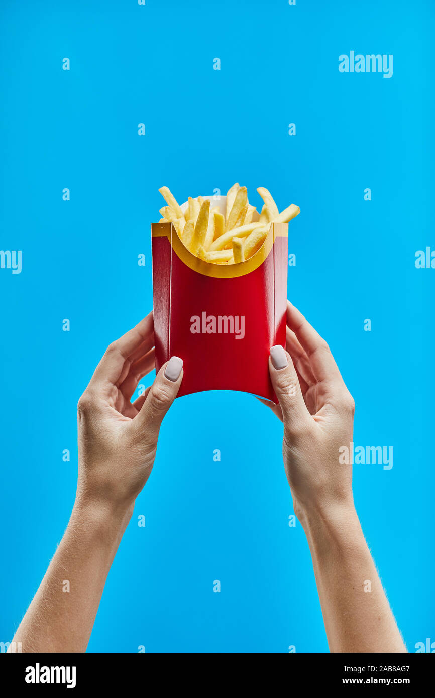 Female hands holding French fries on a blue background Stock Photo - Alamy