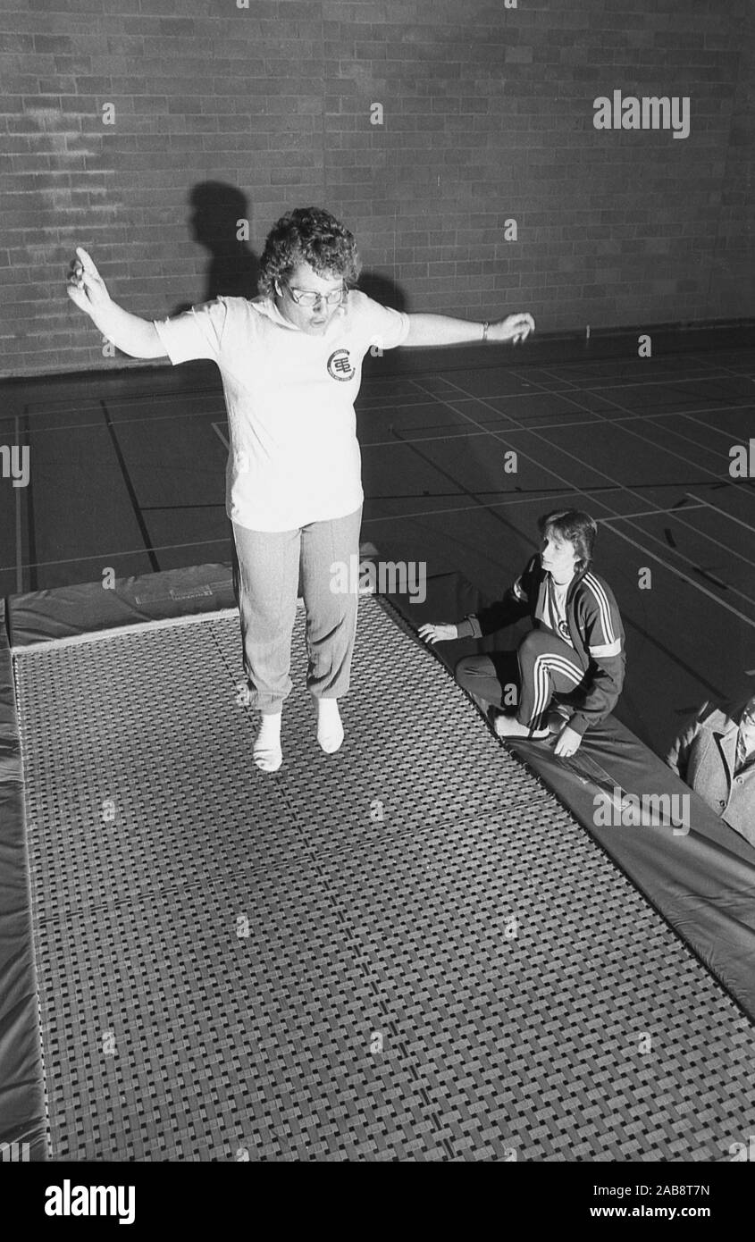 1980s, a middle-aged lady gently exercising, bouncing on a trampoline ...