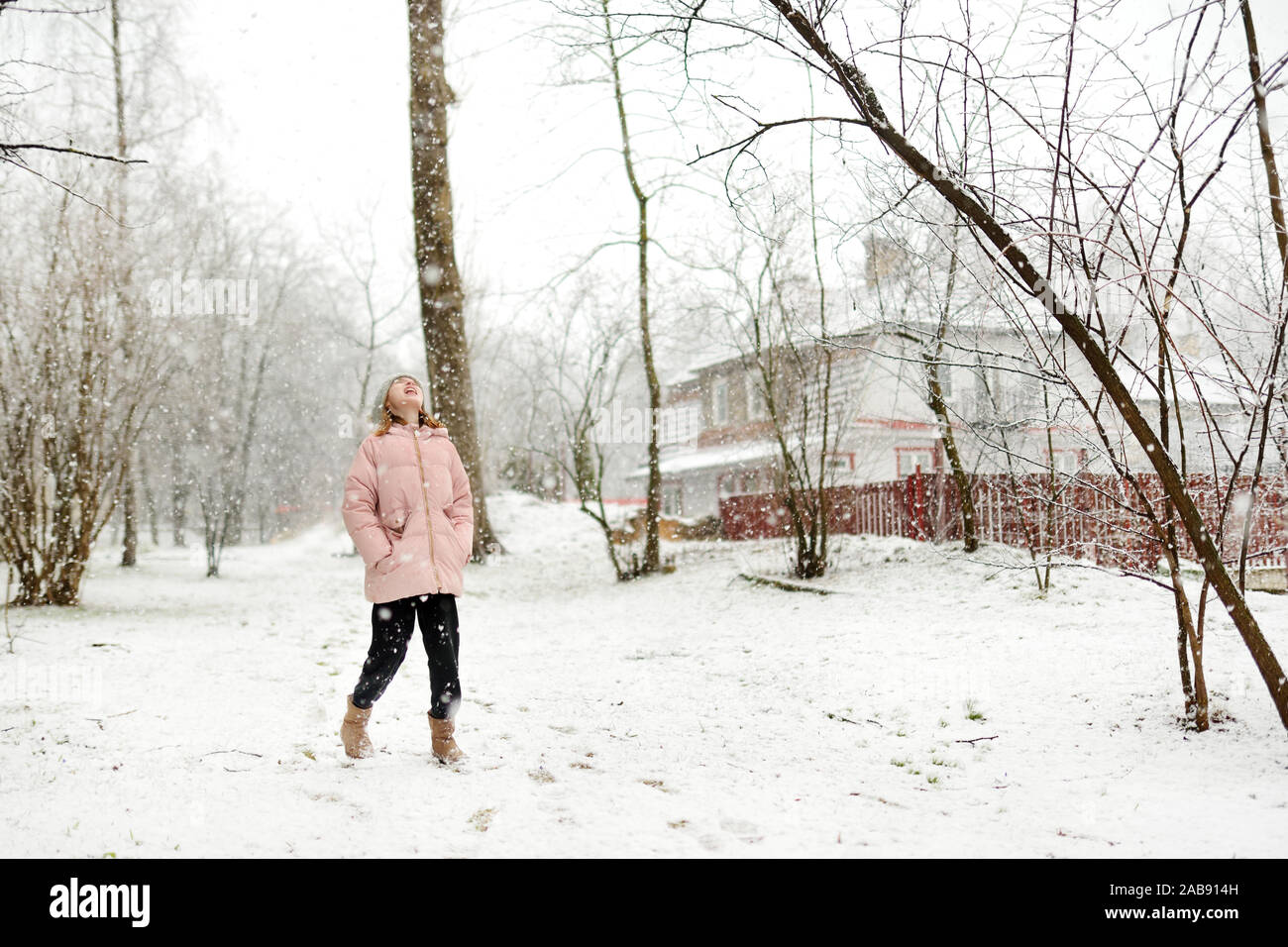 Adorable young girl having fun in beautiful winter park during snowfall ...