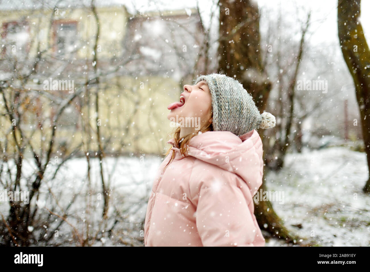 Adorable young girl having fun in beautiful winter park during snowfall ...