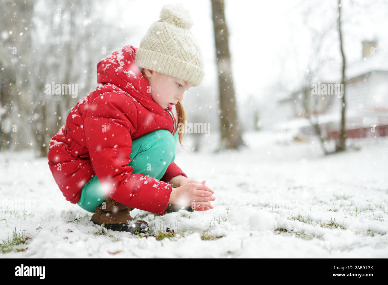 Adorable young girl having fun in beautiful winter park during snowfall ...