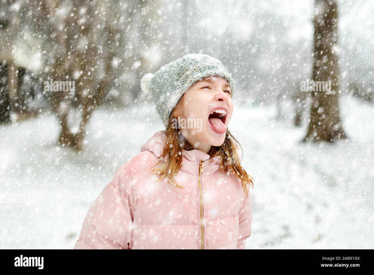 Adorable young girl catching snowflakes with her tongue in beautiful ...