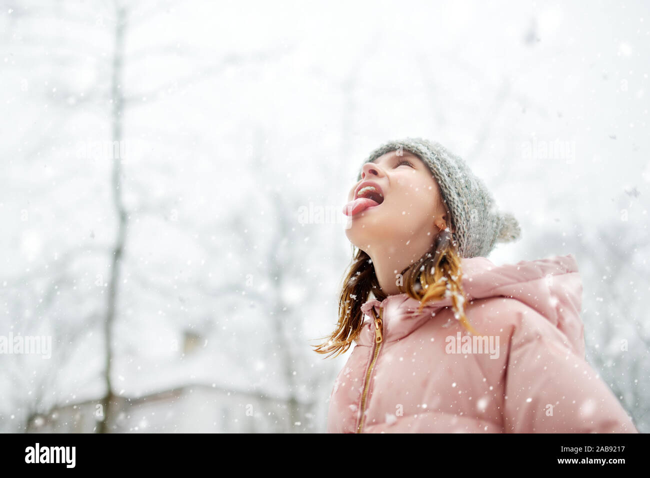 Adorable young girl catching snowflakes with her tongue in beautiful ...