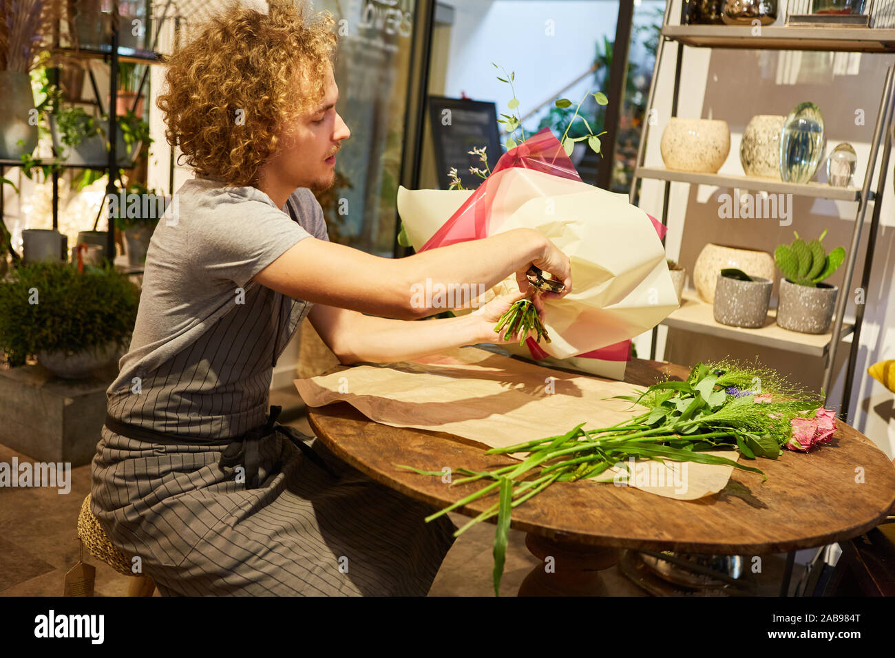 Florist cuts bouquet and packs it in paper in flower shop Stock Photo ...