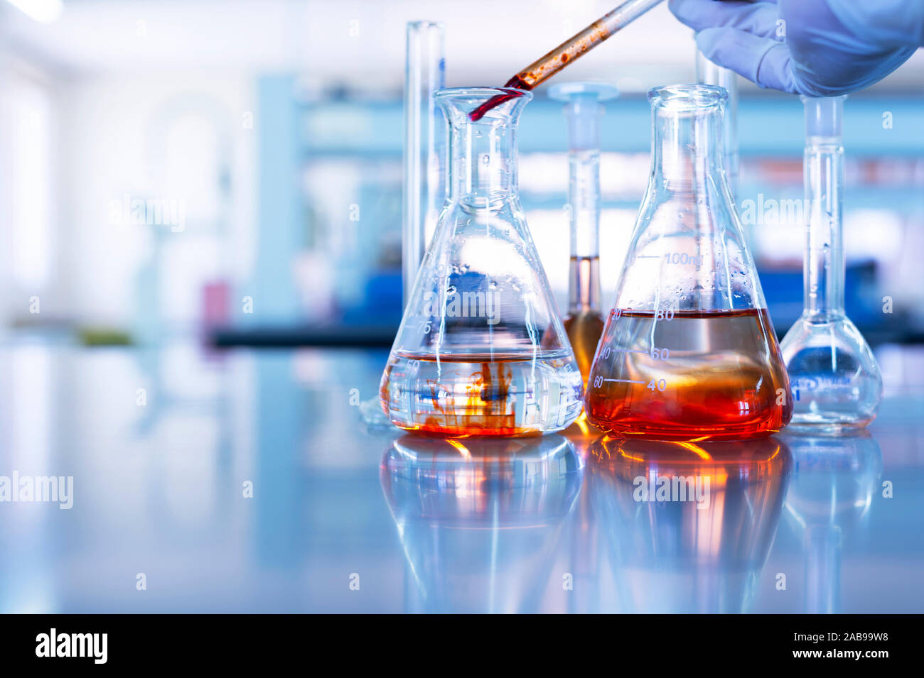 hand of scientist drop orange solution by pipette in glass flask in ...