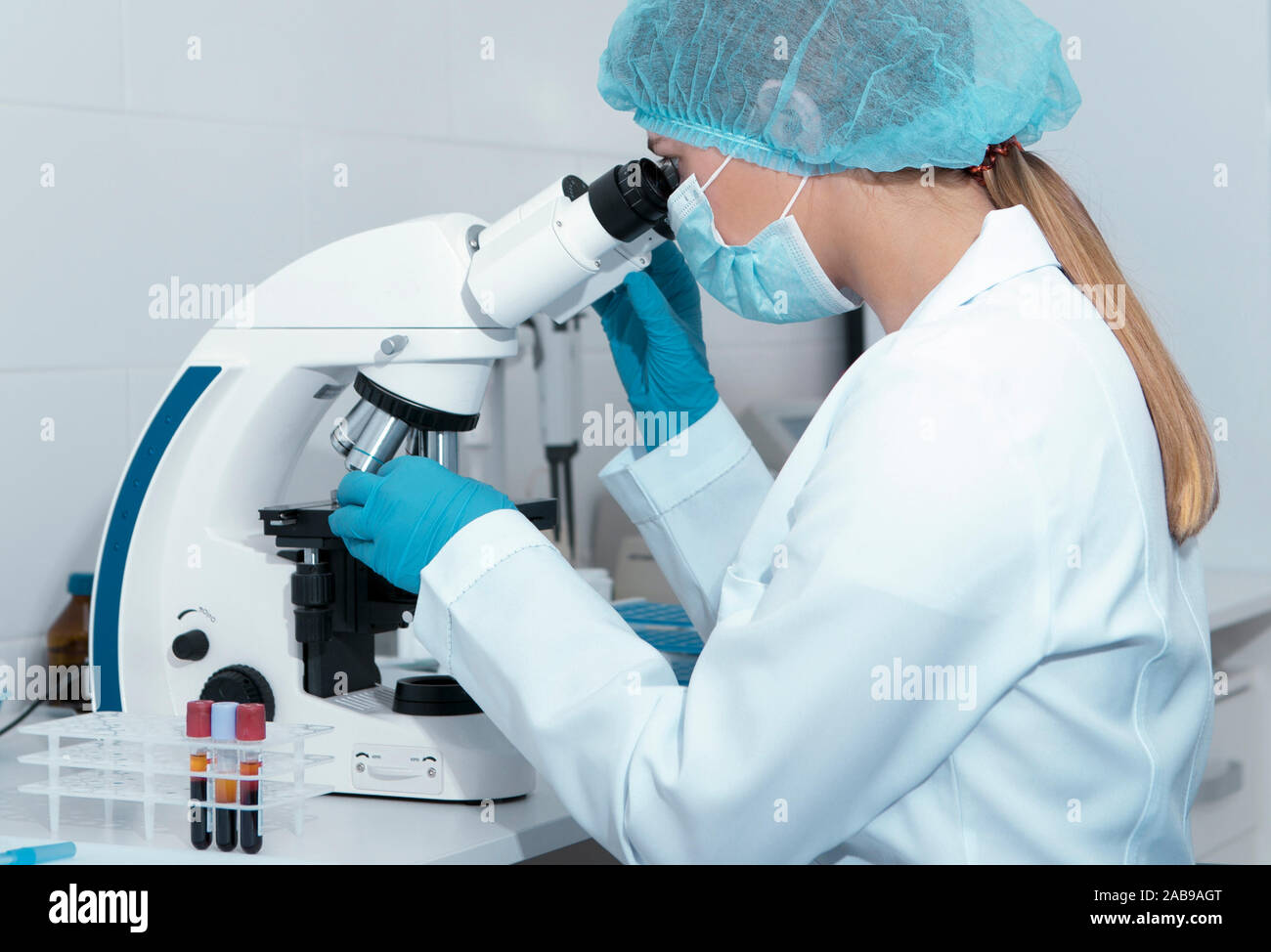 Young female scientist studying new substance or virus in microscope ...
