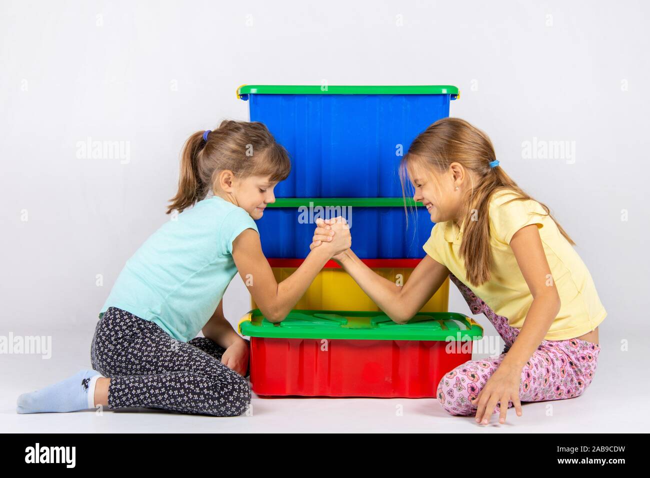Two girls fight on hands, putting elbows on a box with toys Stock Photo ...