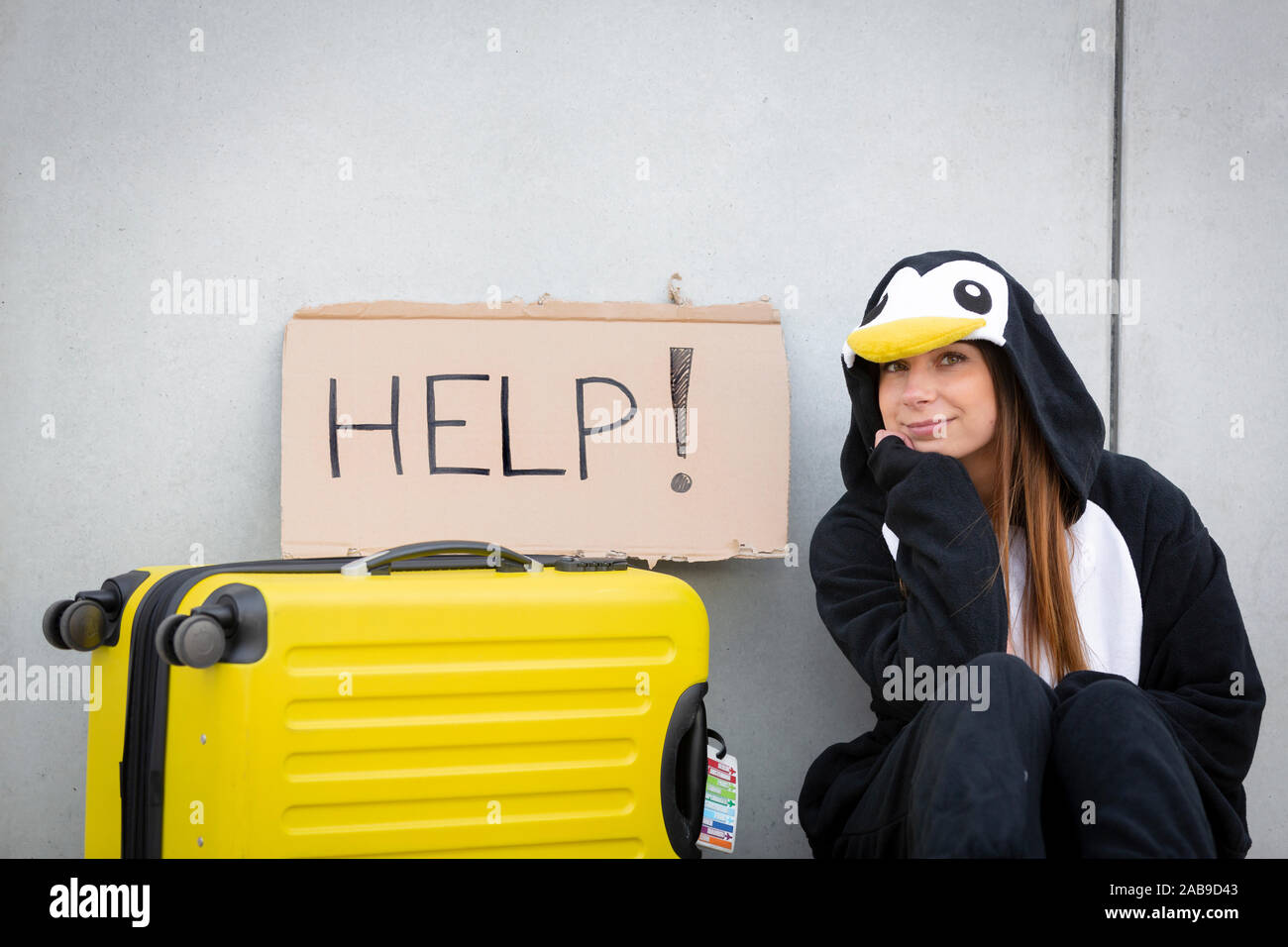 Young woman, with penguin costume and yellow suitcase, has to travel ...