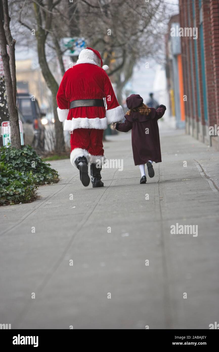 Santa Claus walking down a city sidewalk holding hands with a cute ...
