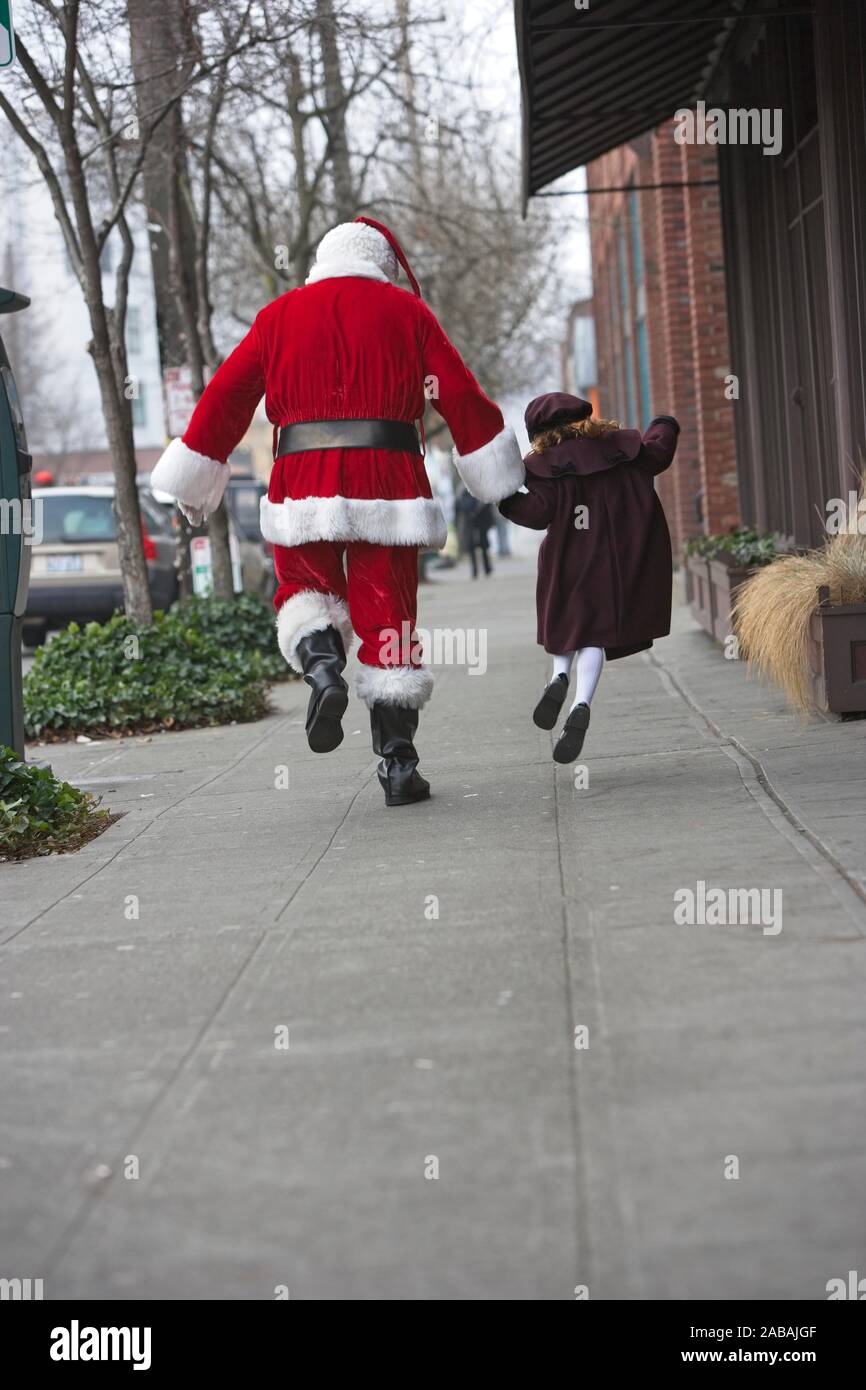 Santa Claus skipping down and urban sidewalk holding hands with a ...