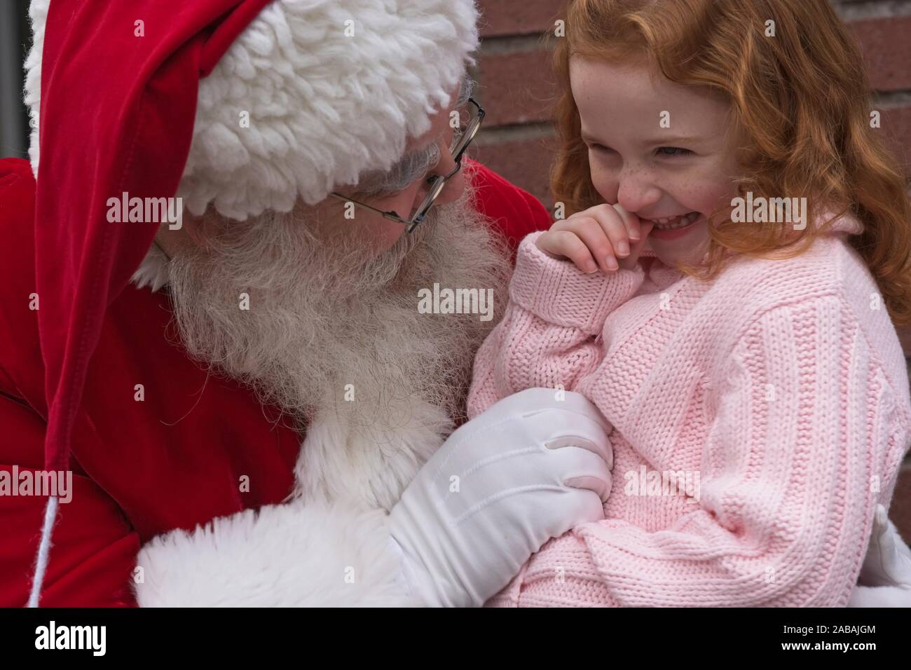 Santa Claus whispering to a shy little redheaded girl Stock Photo - Alamy