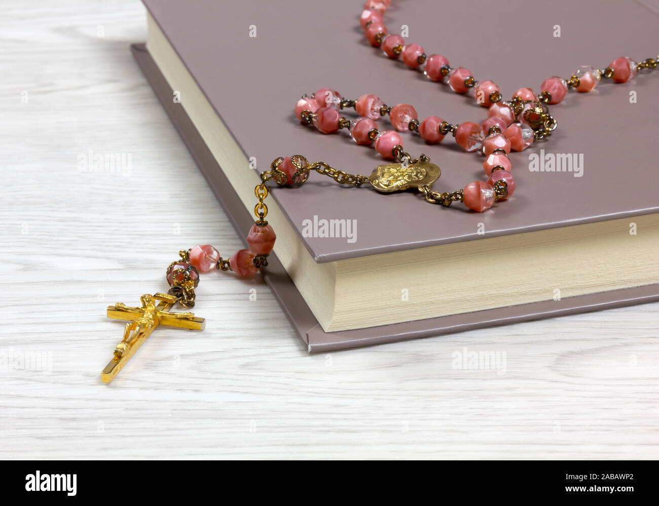 Rosary with pink colored grains lying on a book on a white wooden table ...