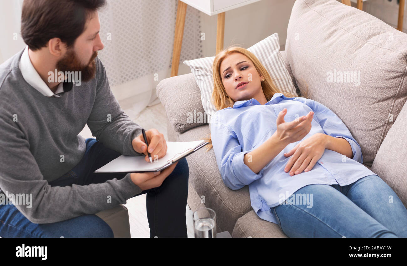 Stressed patient on sofa talking to psychologist at consultation Stock ...