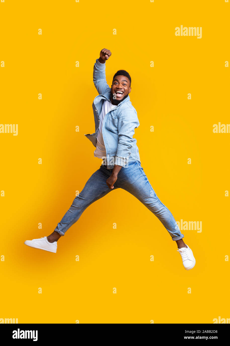 Full length of funny afro guy jumping against yellow studio background ...