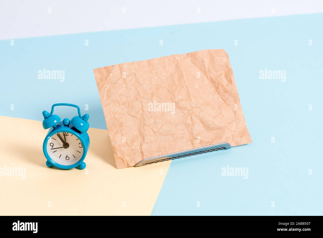 Mini size alarm clock beside a Paper sheet placed tilted on pastel ...