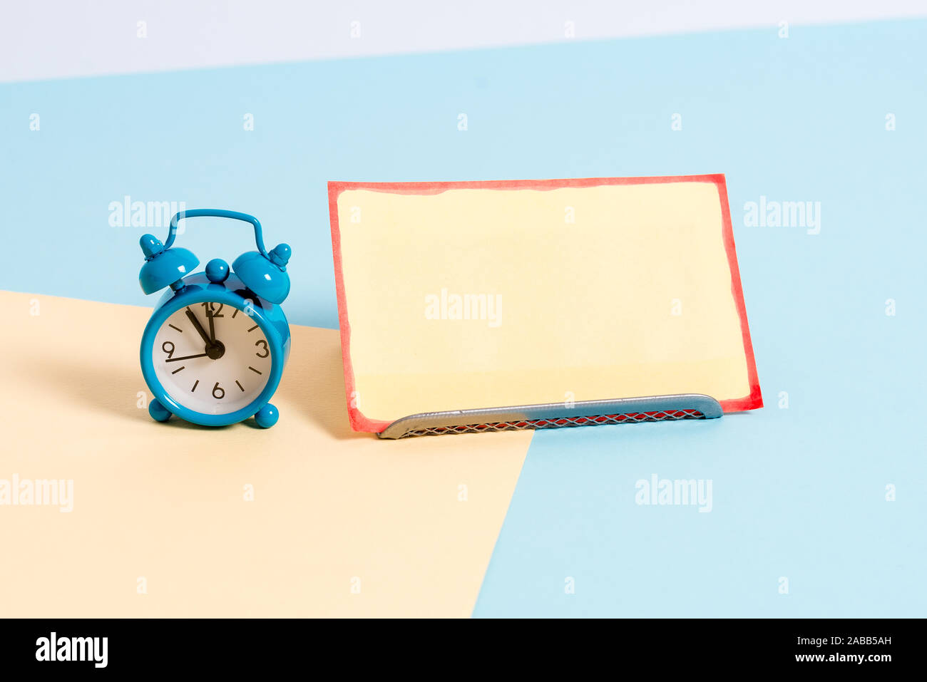 Mini size alarm clock beside a Paper sheet placed tilted on pastel ...