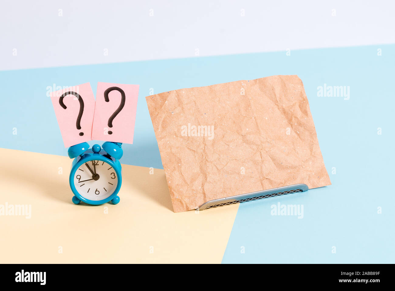 Mini size alarm clock beside a Paper sheet placed tilted on pastel ...