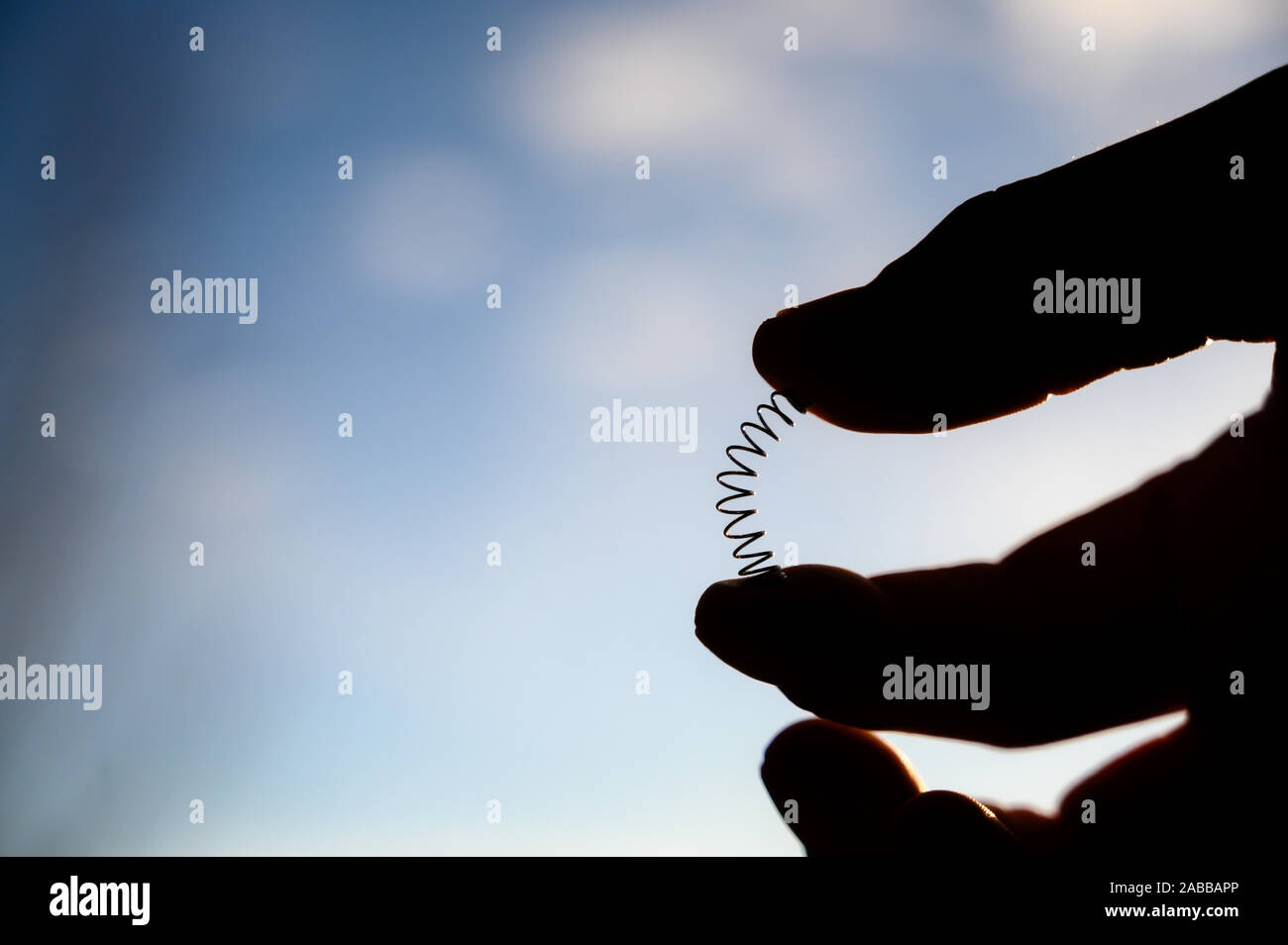 Silhouette of hand compressing a metal spring between a thumb and ...