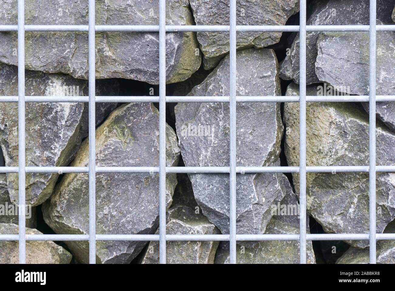 Wall of grey rocks behind a light grey metal grid background Stock ...