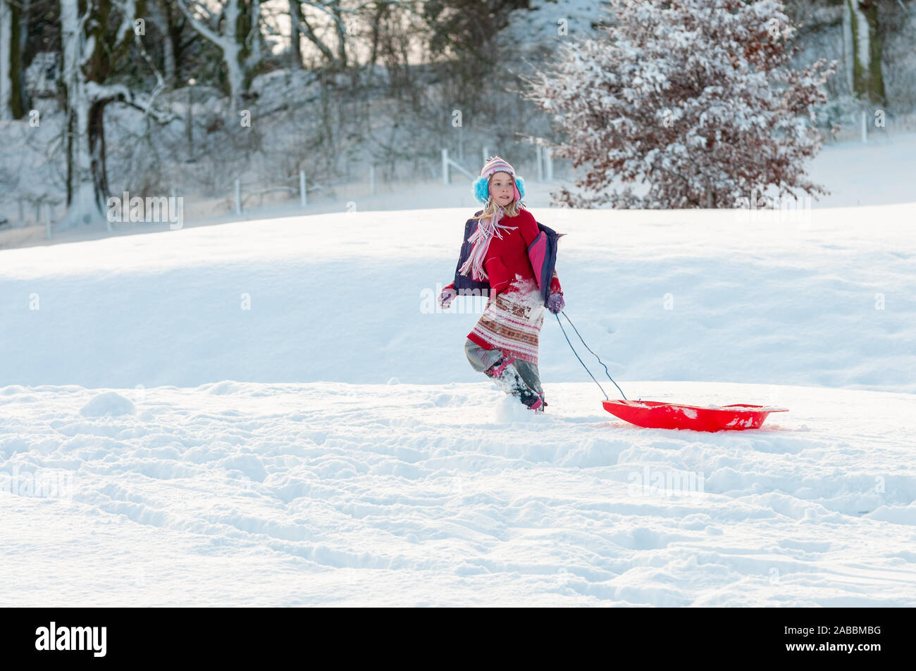 Vibrantly dressed young girl dragging her sled behind her through deep ...