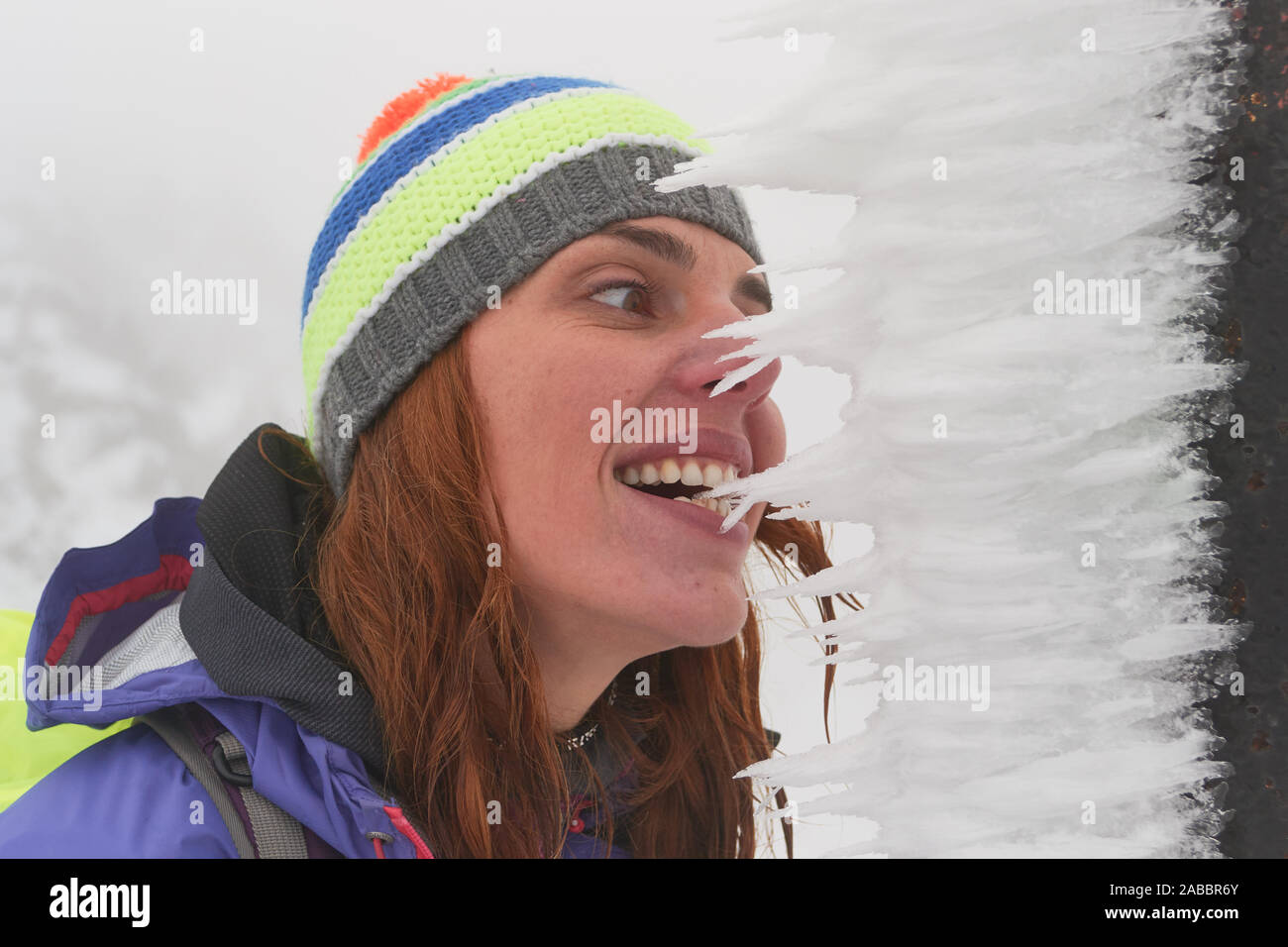 Woman hiker biting on frosted snow, wind blown by heavy winds during a ...
