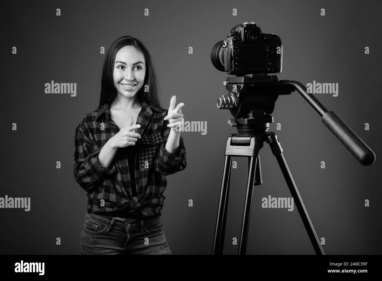 Studio shot of young beautiful hipster woman vlogging in black and ...