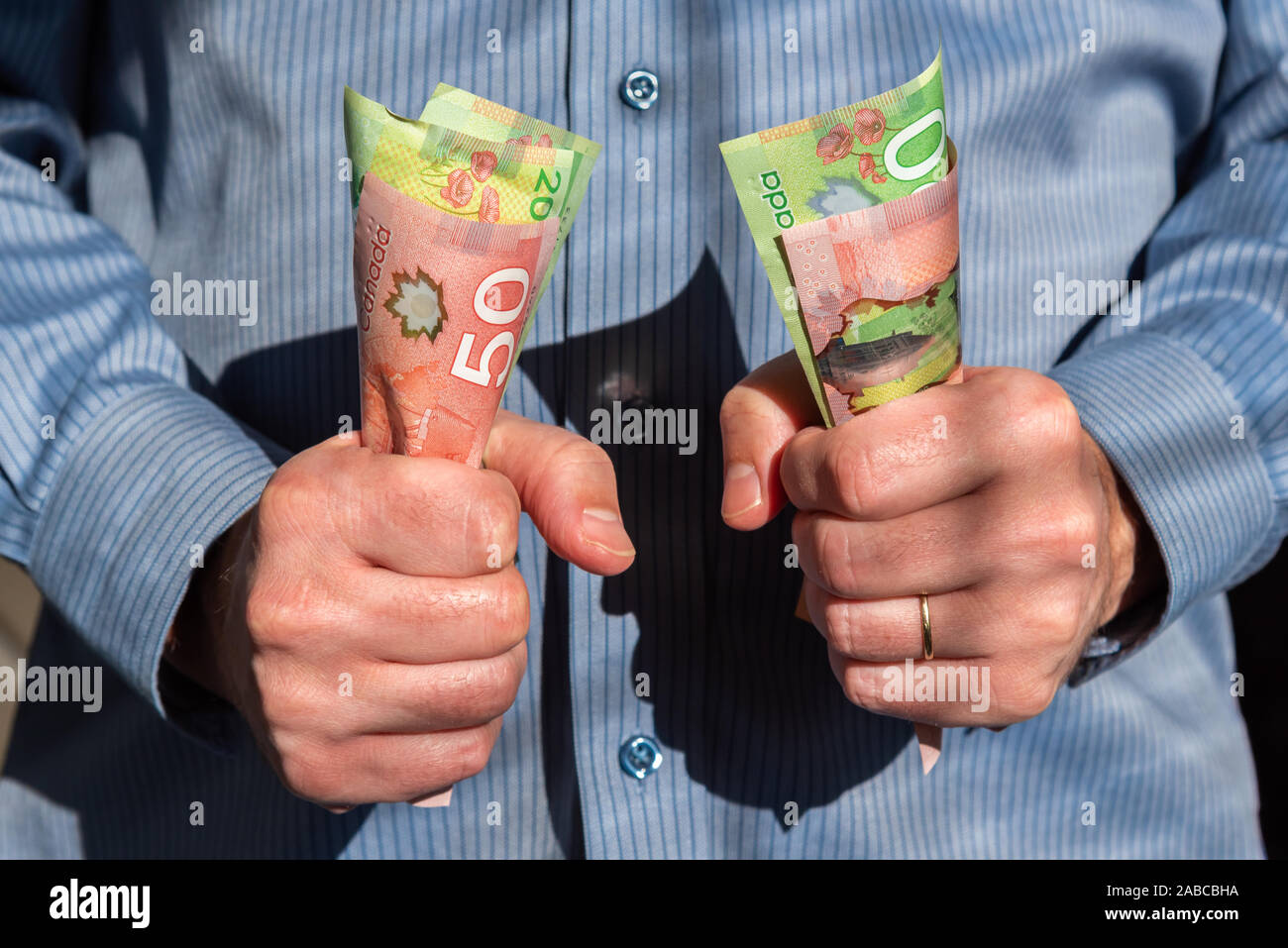 Man tightly holding Canadian twenty and fifty dollar bills in both ...