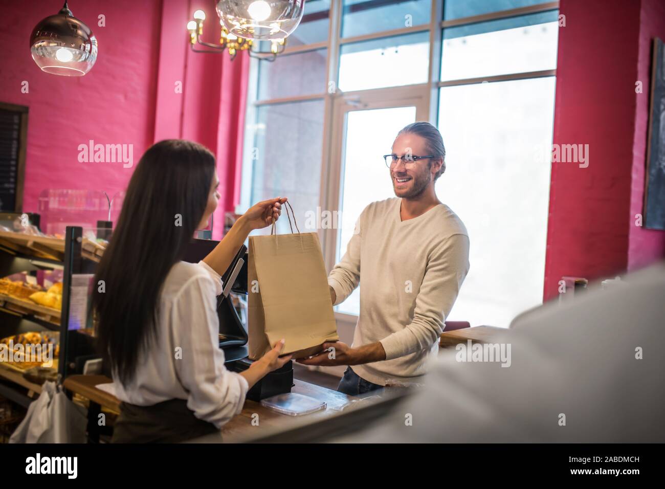Man wearing glasses smiling while talking to cashier and buying pastry ...