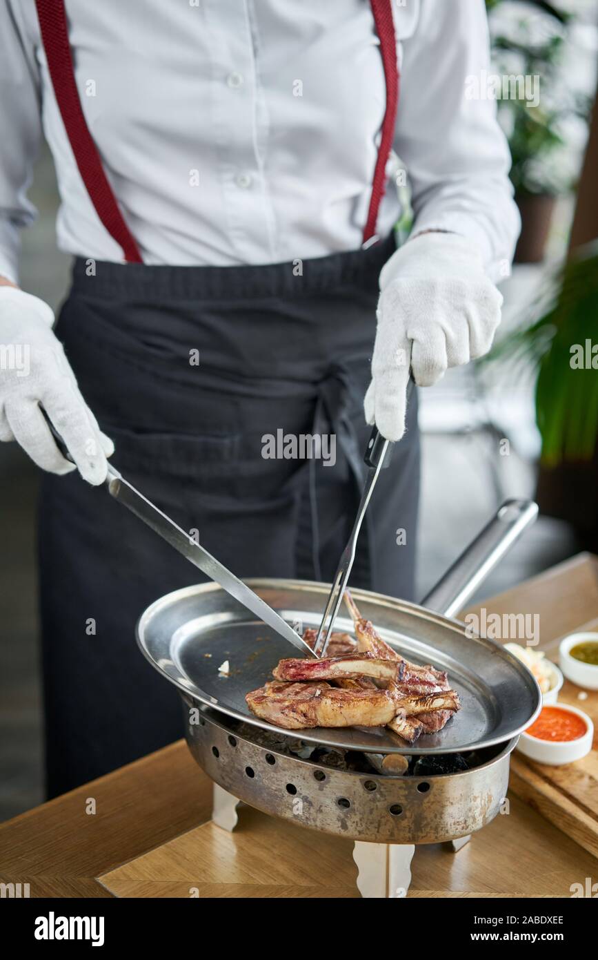 The waiter is butchering with a knife. Rack of lamb , grilled meat with ...
